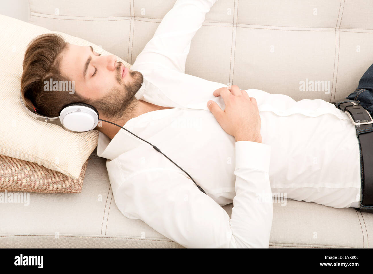 Portrait of a young man relaxing and listening to music on the couch ...