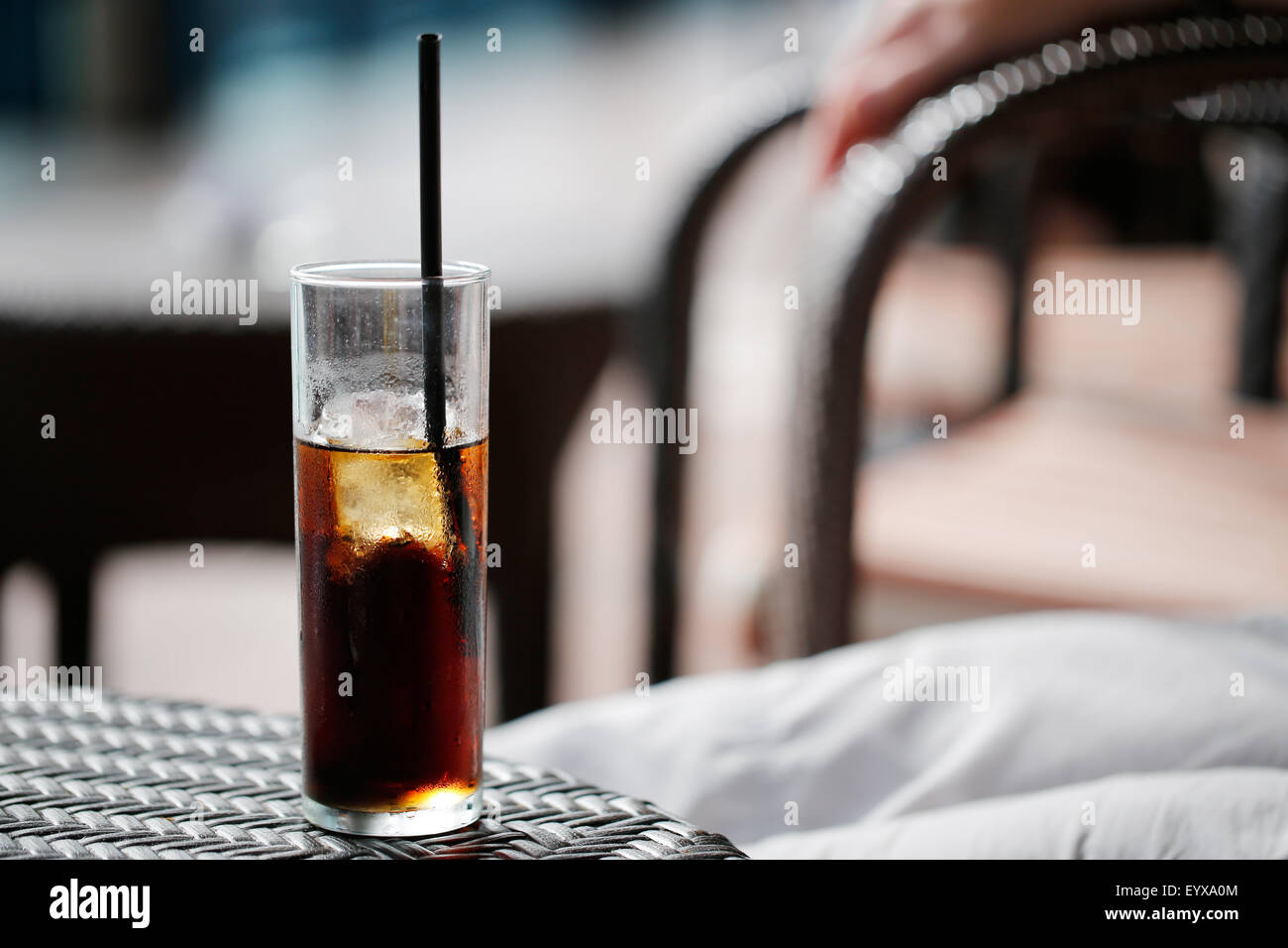 A refreshing tall glass of coke, with ice, on a table. the drink is ...