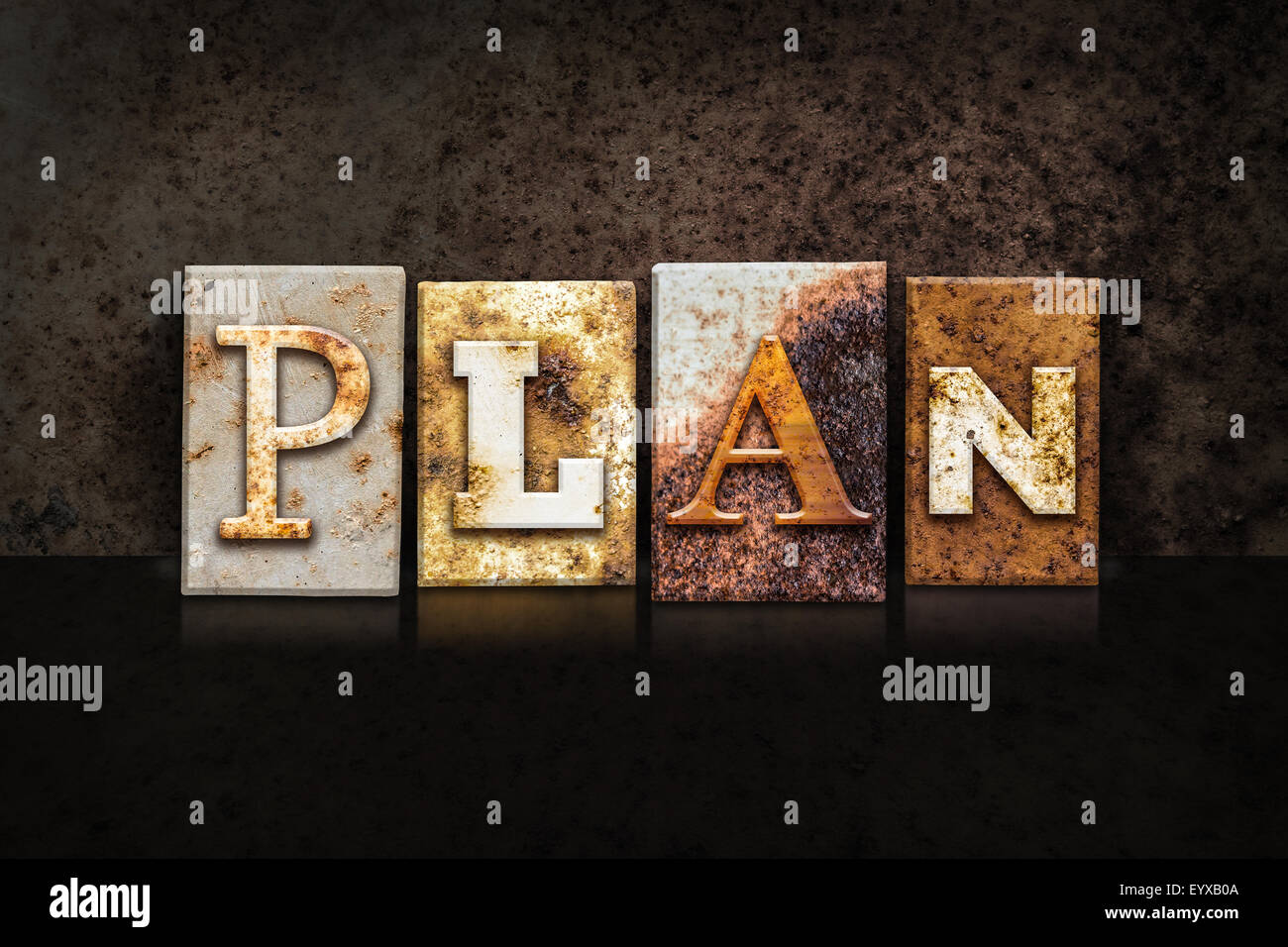 The word "PLAN" written in rusty metal letterpress type on a dark ...