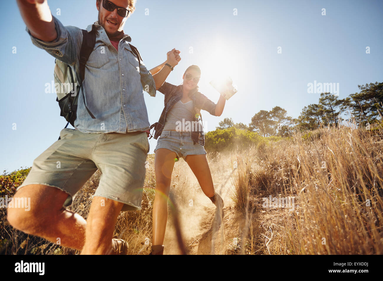 Portrait of happy young couple having fun on their hiking trip, sliding down the mountain trail ...