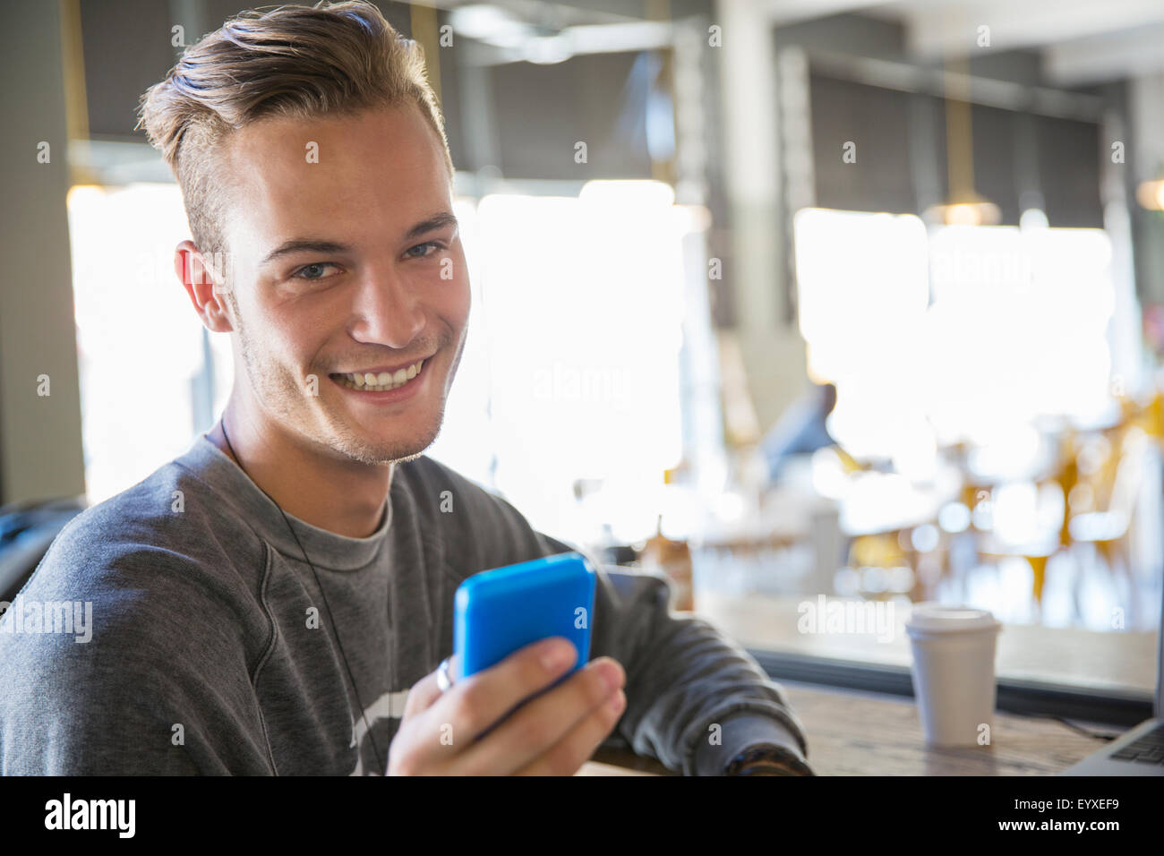 Portrait smiling young man texting with cell phone in cafe Stock Photo ...