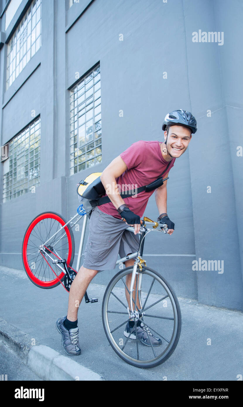Portrait smiling bicycle messenger with helmet leaning forward on urban ...