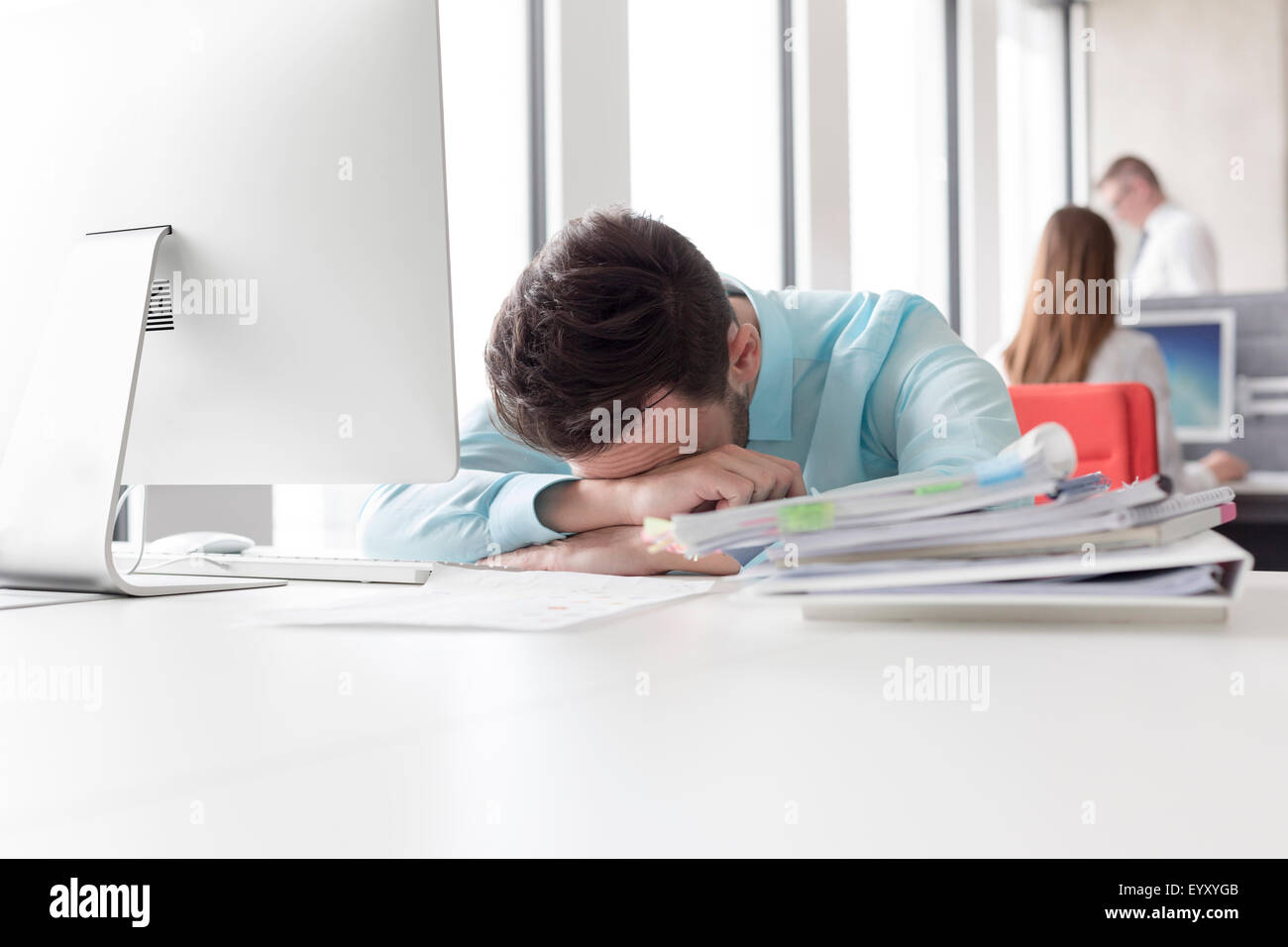 Frustrated businessman with head down next to stack of reports on desk ...