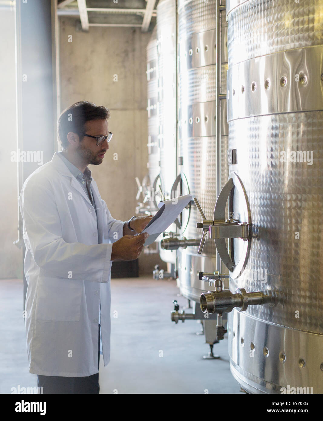 Vintner in lab coat with clipboard checking stainless steel vat in ...