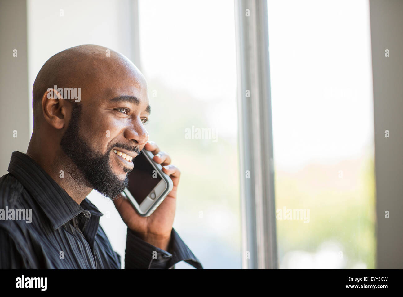 Black man talking on cell phone near window Stock Photo - Alamy