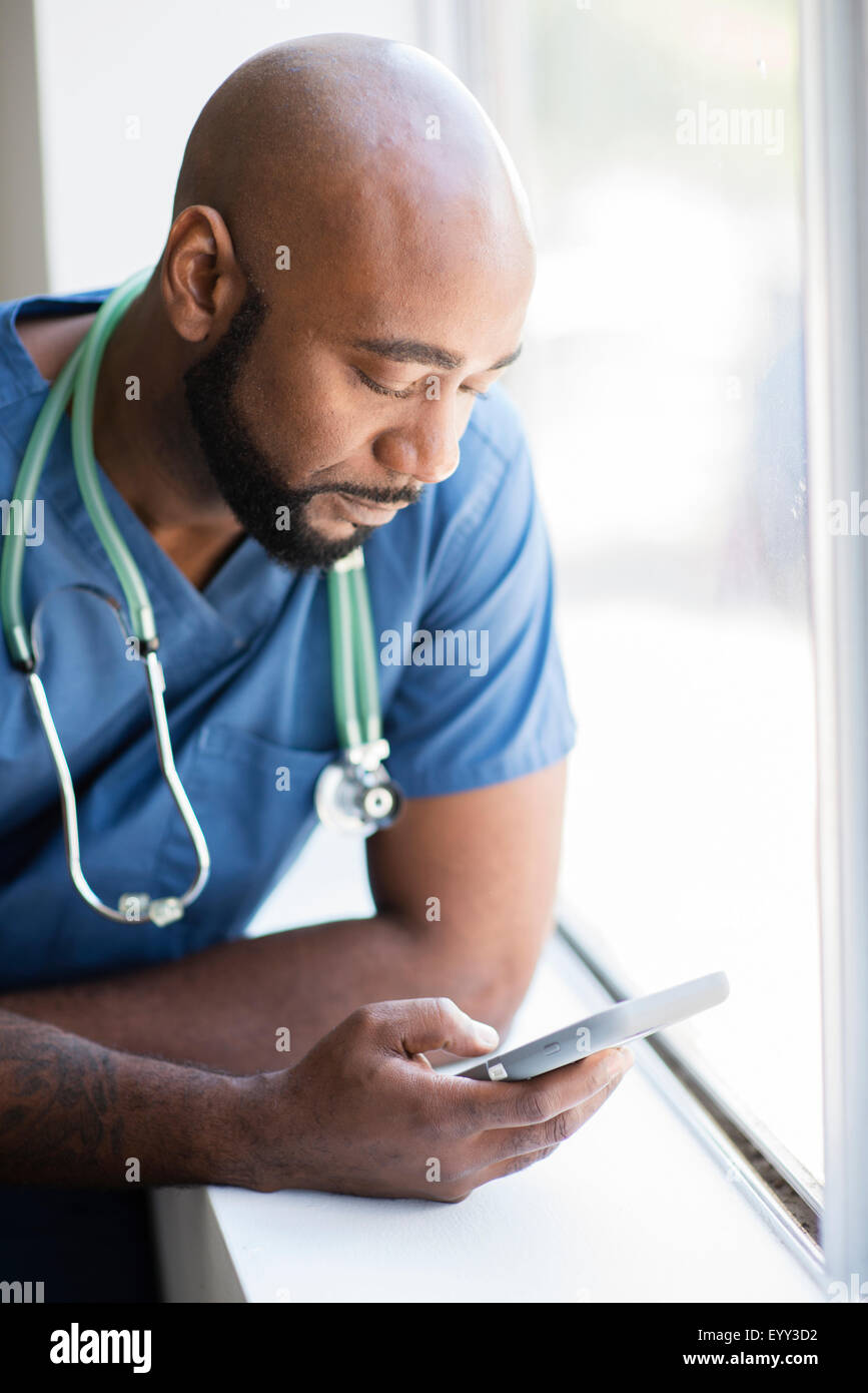 Black nurse using cell phone near window Stock Photo - Alamy