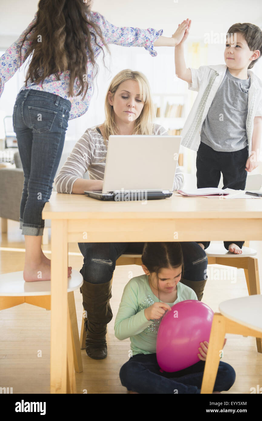 Caucasian mother using laptop with chaotic children Stock Photo - Alamy
