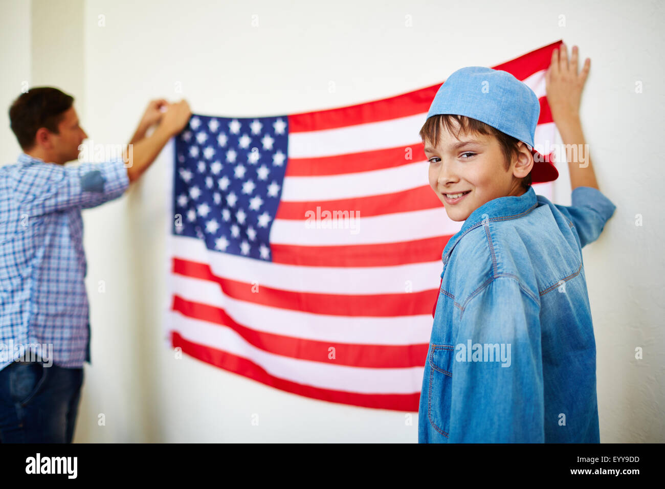 Handsome boy looking at camera while holding USA flag hanging on wall ...