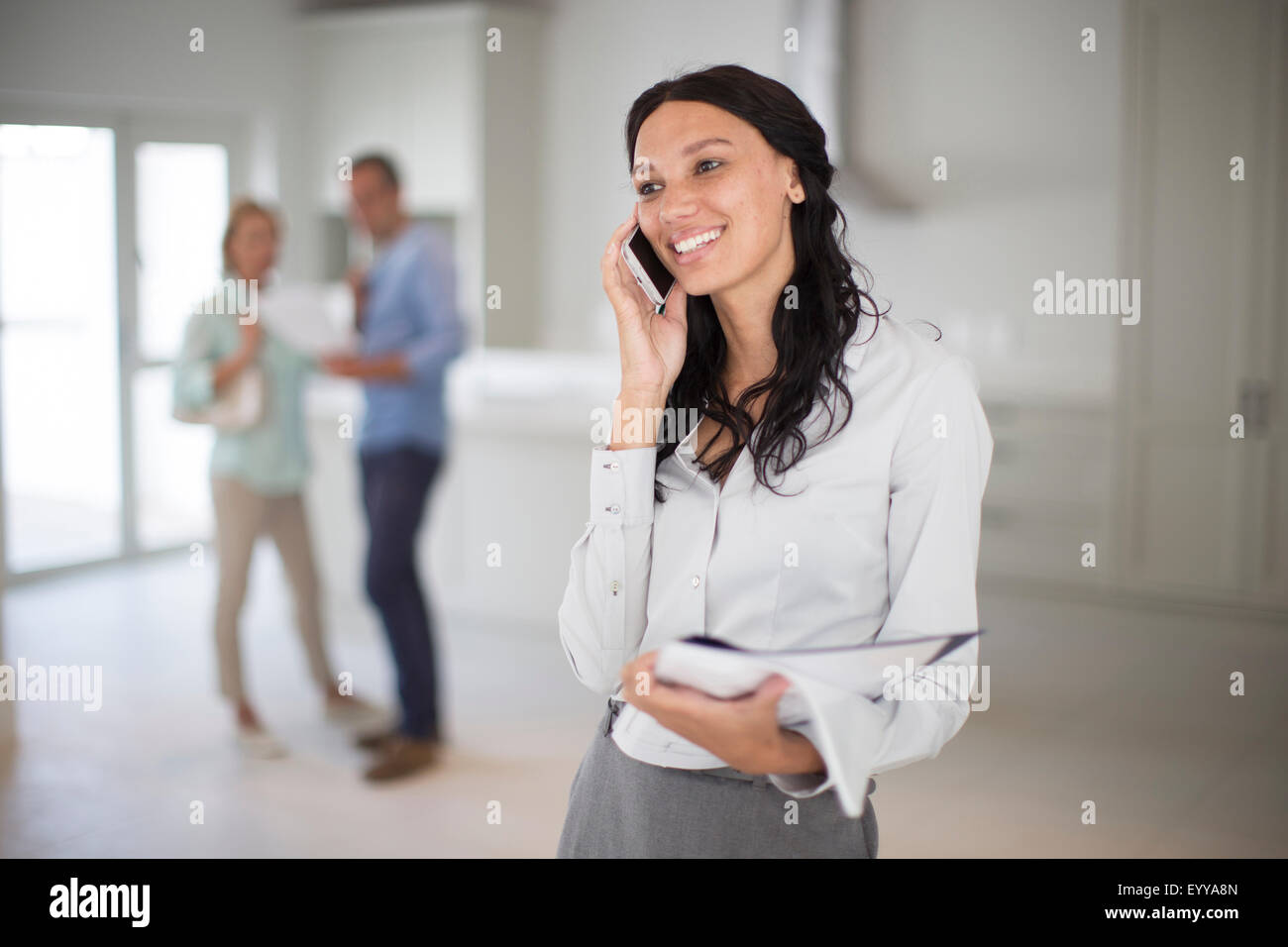 Realtor talking on cell phone with couple in new home Stock Photo - Alamy
