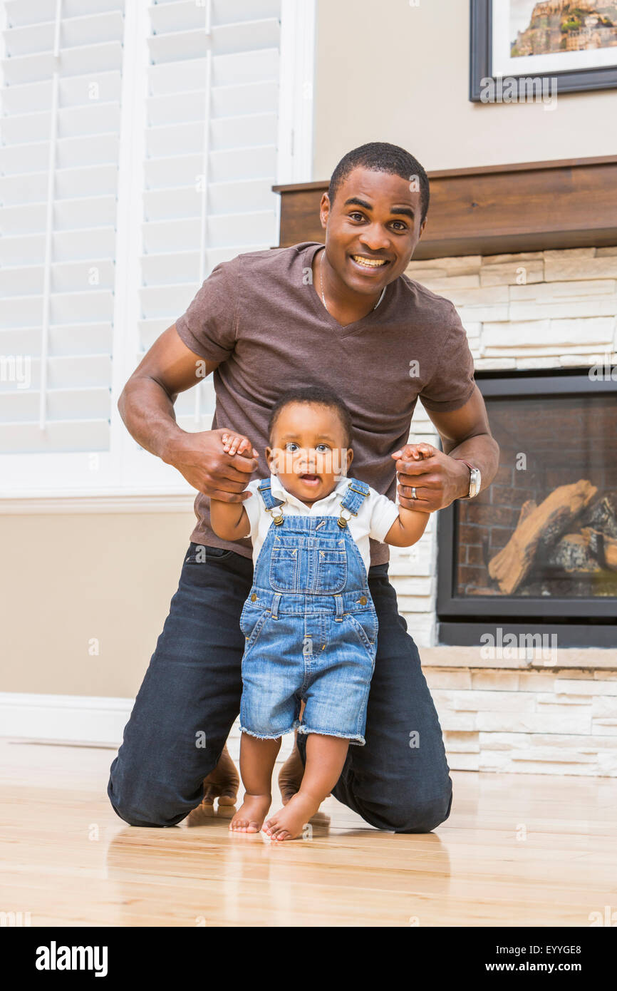 Black father helping baby son walk on living room floor Stock Photo - Alamy