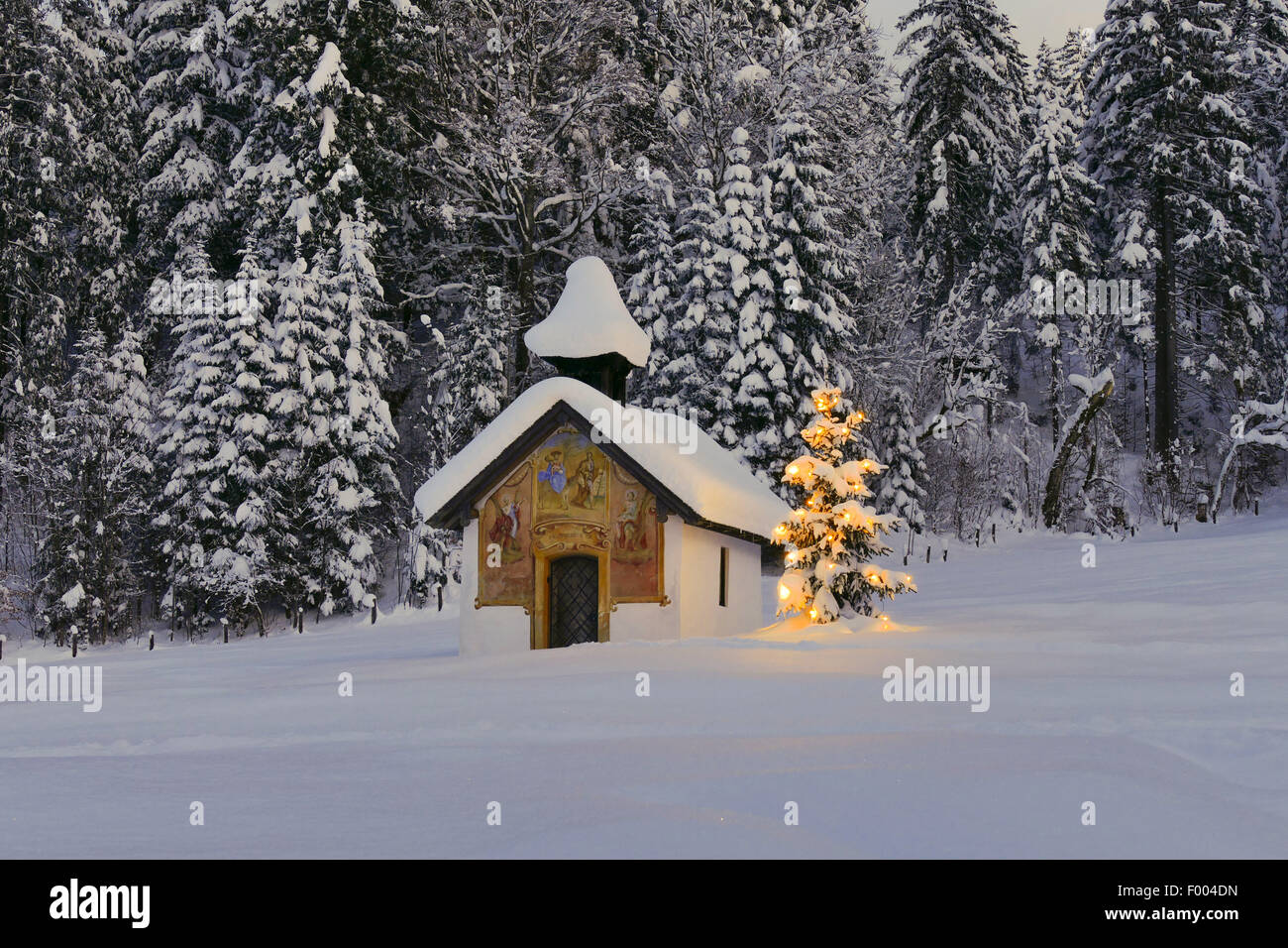 illuminated christmas tree in front of a chapel in snow landscape ...