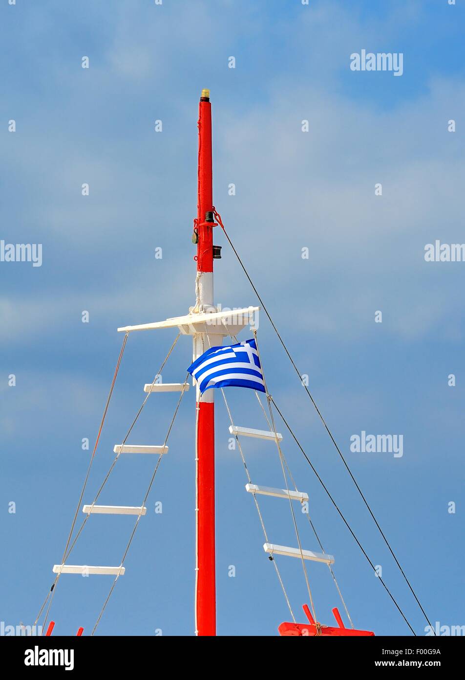 A red mast on a yacht flying the Greek Flag against a blue sky ...