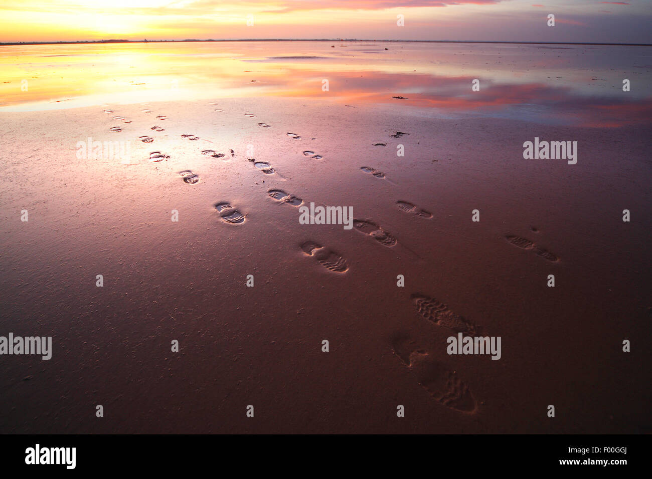 footprints on the beach at outgoing tide and reflection of clouds ...