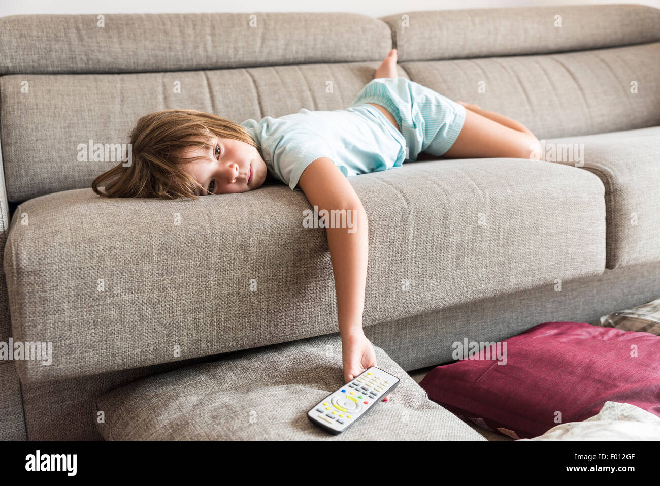 Little girl watching TV on the couch stretched Stock Photo - Alamy