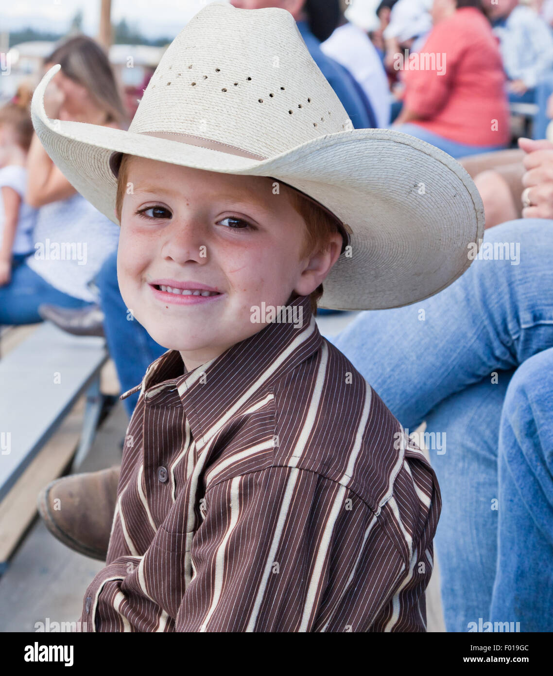 A cute little cowboy with a dirty face sits in a crowd of people ...