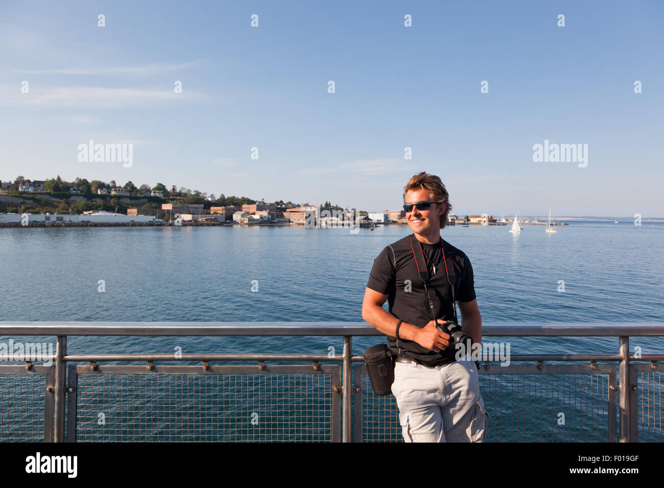 A smiling young man with a camera casually leaning against a railing on ...