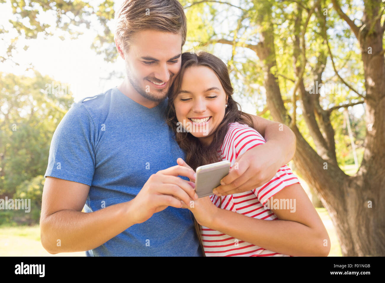 Cute couple using mobile phone in the park Stock Photo - Alamy