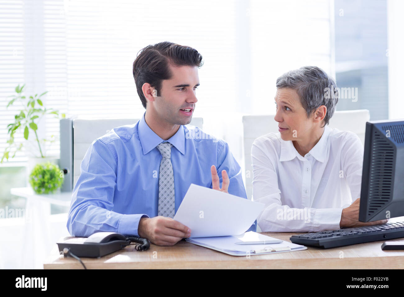 Two business people looking at a paper while working on folder Stock ...