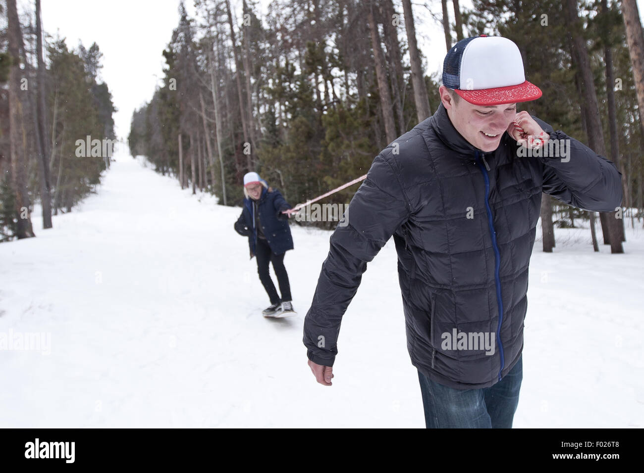 Young man pulling man on snowboard with rope Stock Photo - Alamy