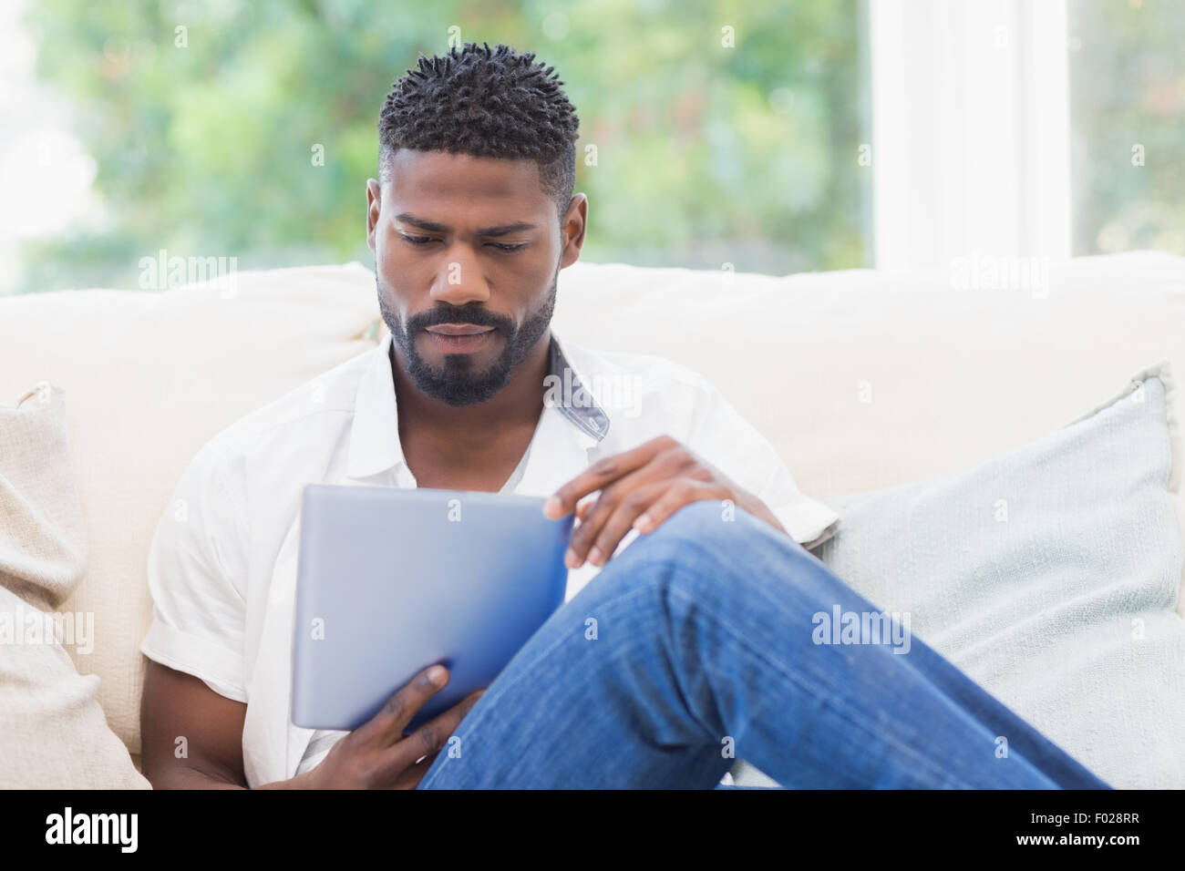 Man using his tablet on couch Stock Photo - Alamy