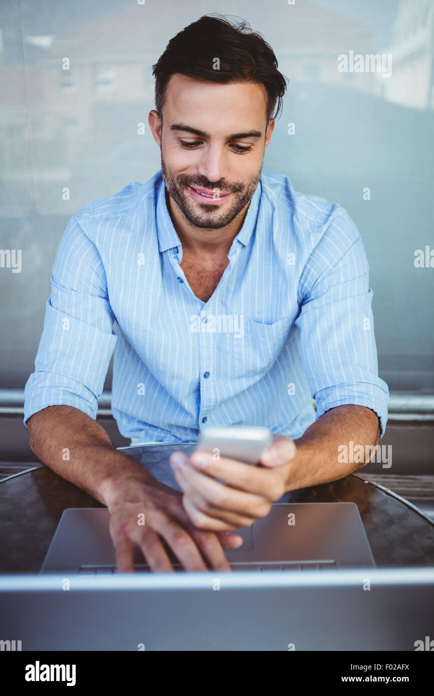 Smiling businessman using phone while working on laptop Stock Photo - Alamy