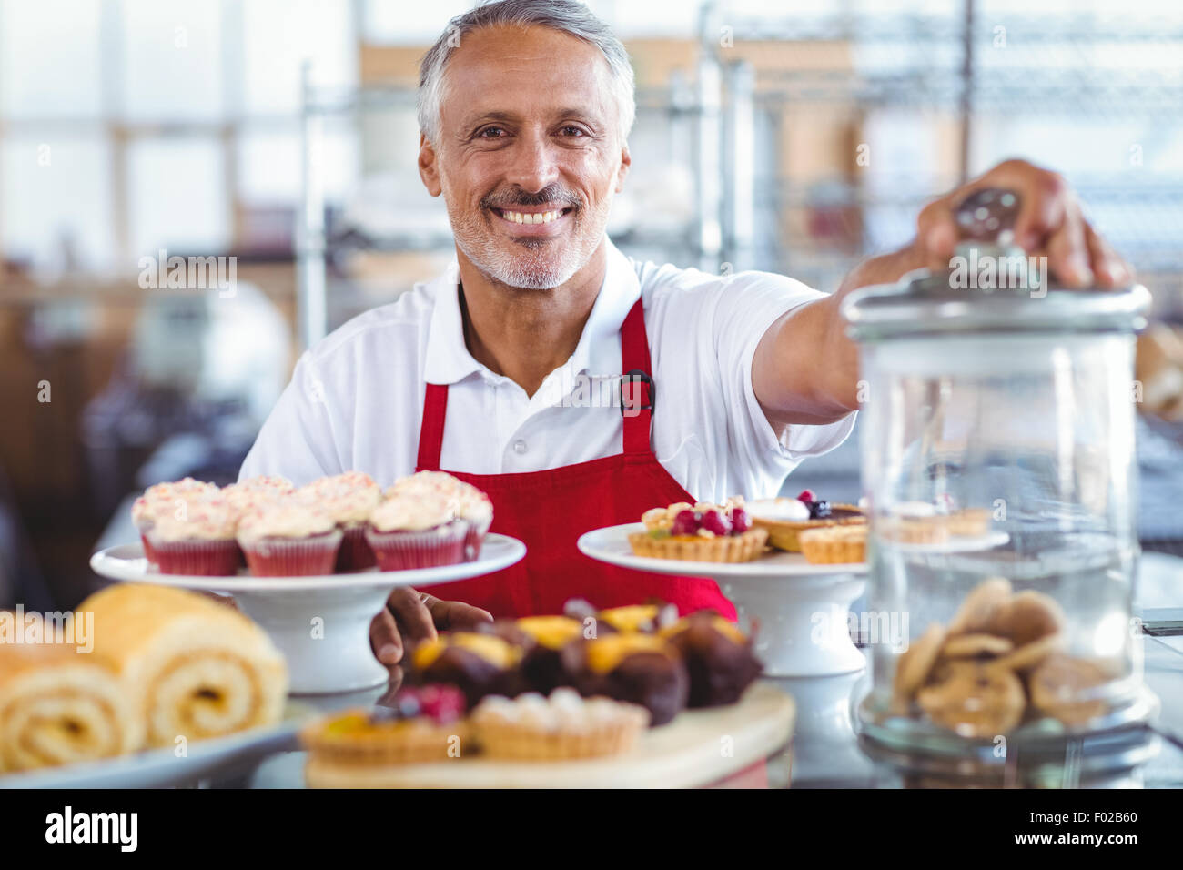 Happy barista smiling at camera behind plates of cakes Stock Photo - Alamy
