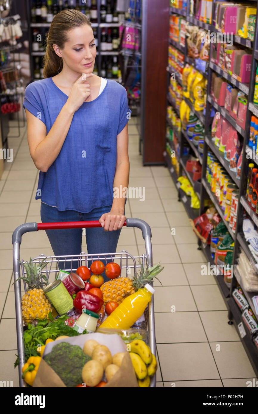 Thoughtful pretty woman pushing trolley in aisle Stock Photo - Alamy