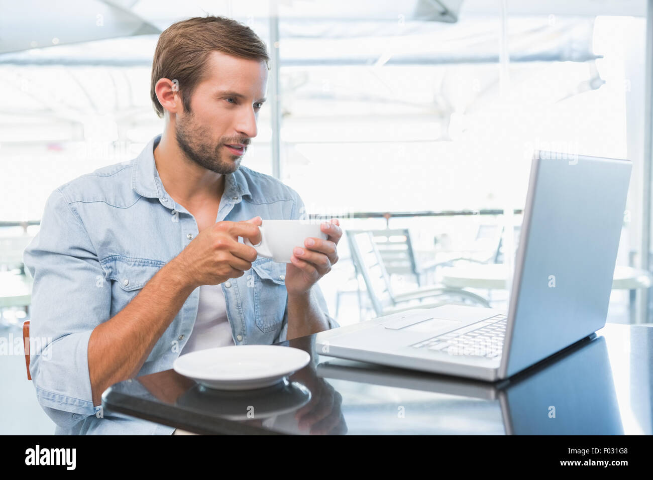 Young happy man holding his coffee while looking at his laptop Stock ...