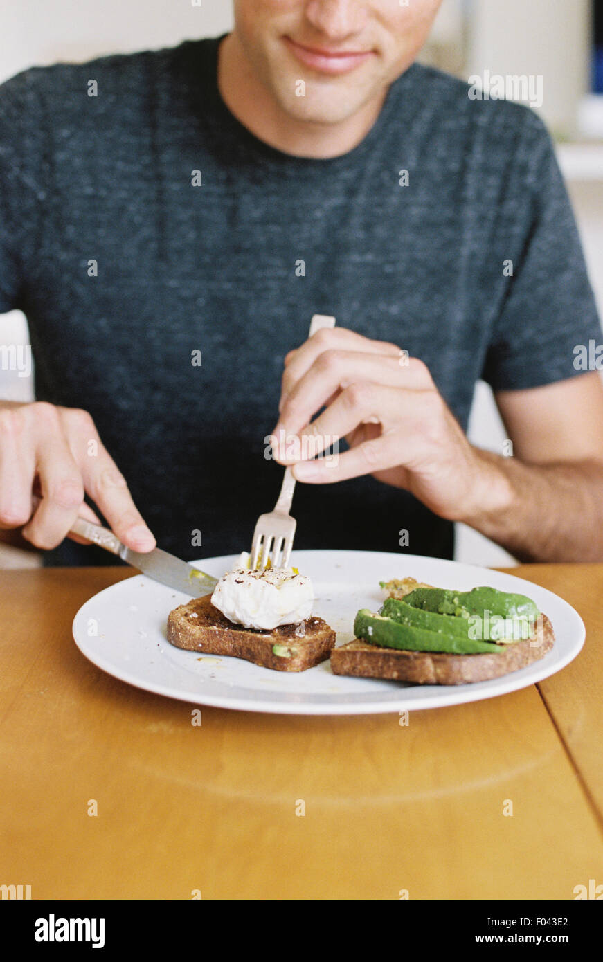 Man sitting in front of a plate of food at a table, eating Stock Photo ...