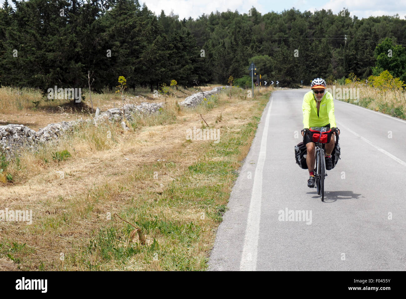 A touring cyclist riding a bicycle on a country road along a low stone ...