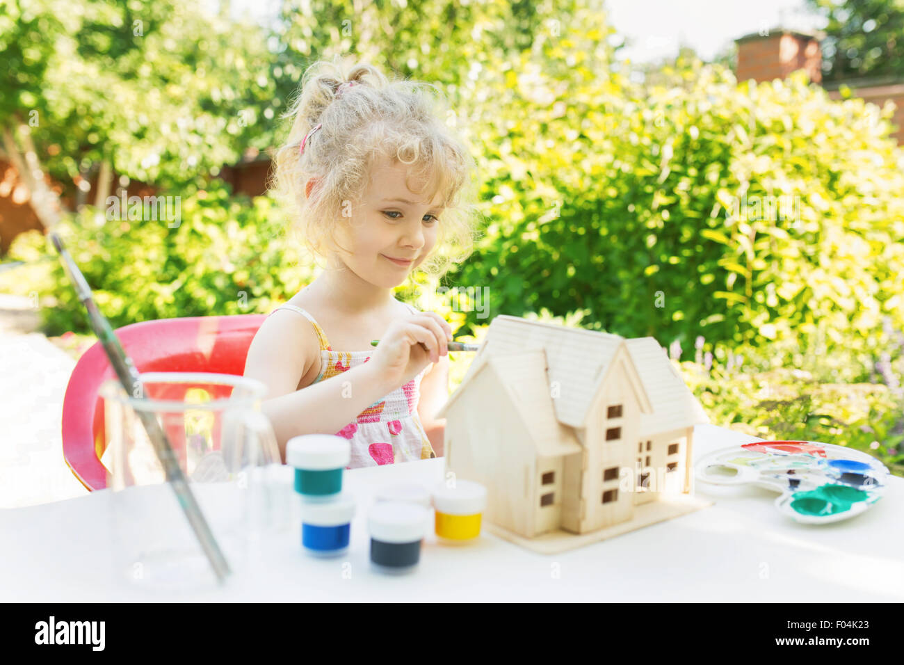 Llittle girl paints wooden model of house, summer outdoor, new home ...