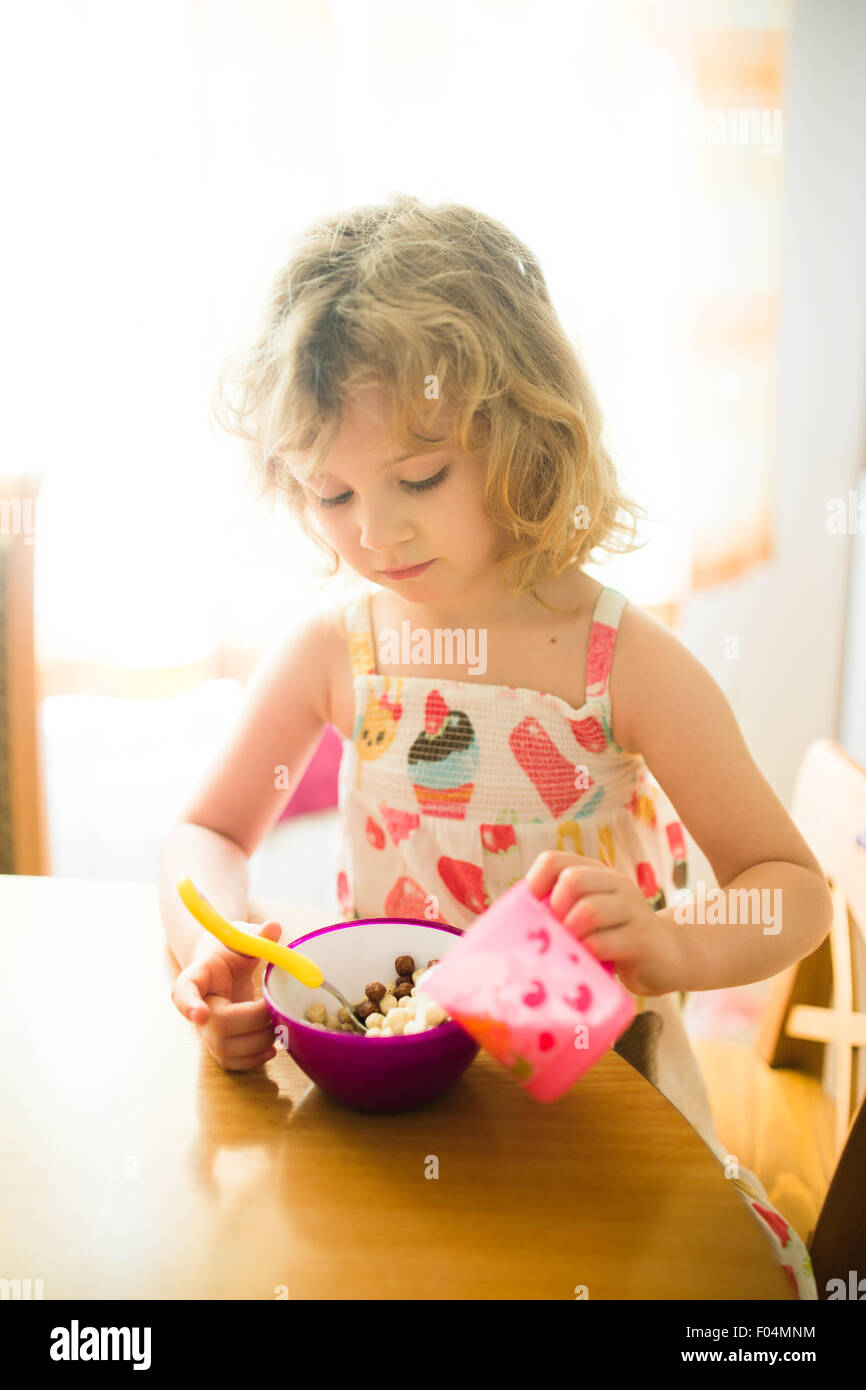 Little girl eating corn balls in the kitchen. Morning light Stock Photo ...