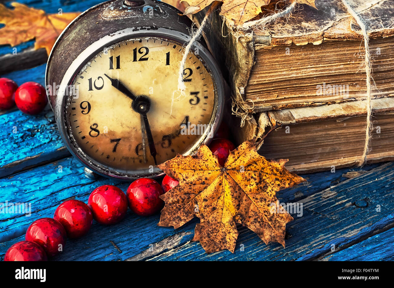 Obsolete alarm clock on background of old books and yellow maple leaf ...
