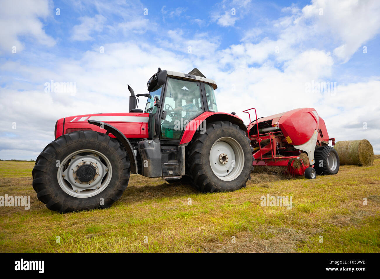 huge tractor collecting haystack in the field at nice blue sunny day ...