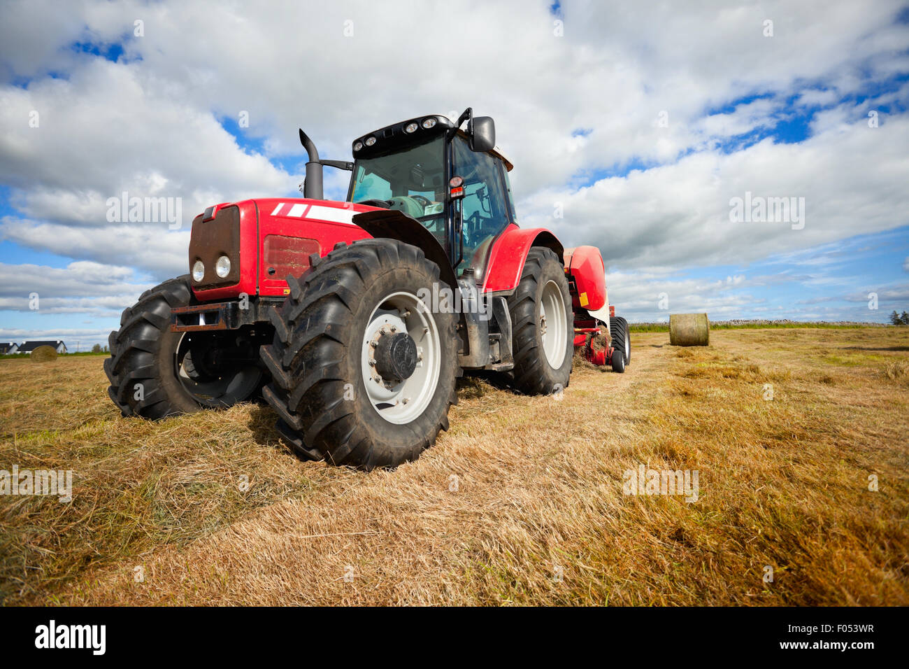 huge tractor collecting haystack in the field in a nice blue sunny day ...
