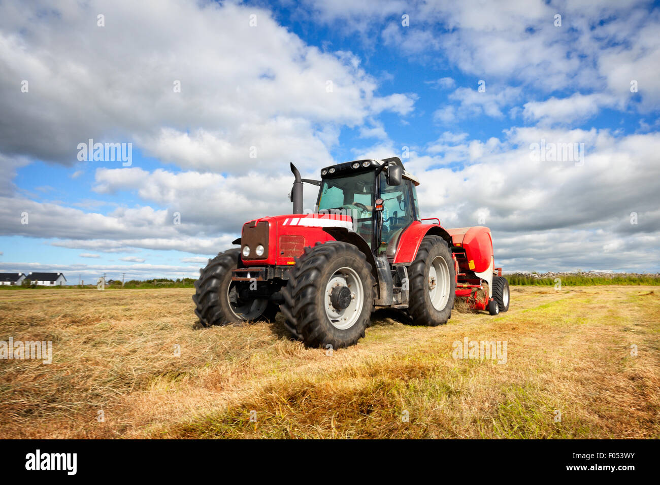 huge tractor collecting haystack in the field at nice blue sunny day ...