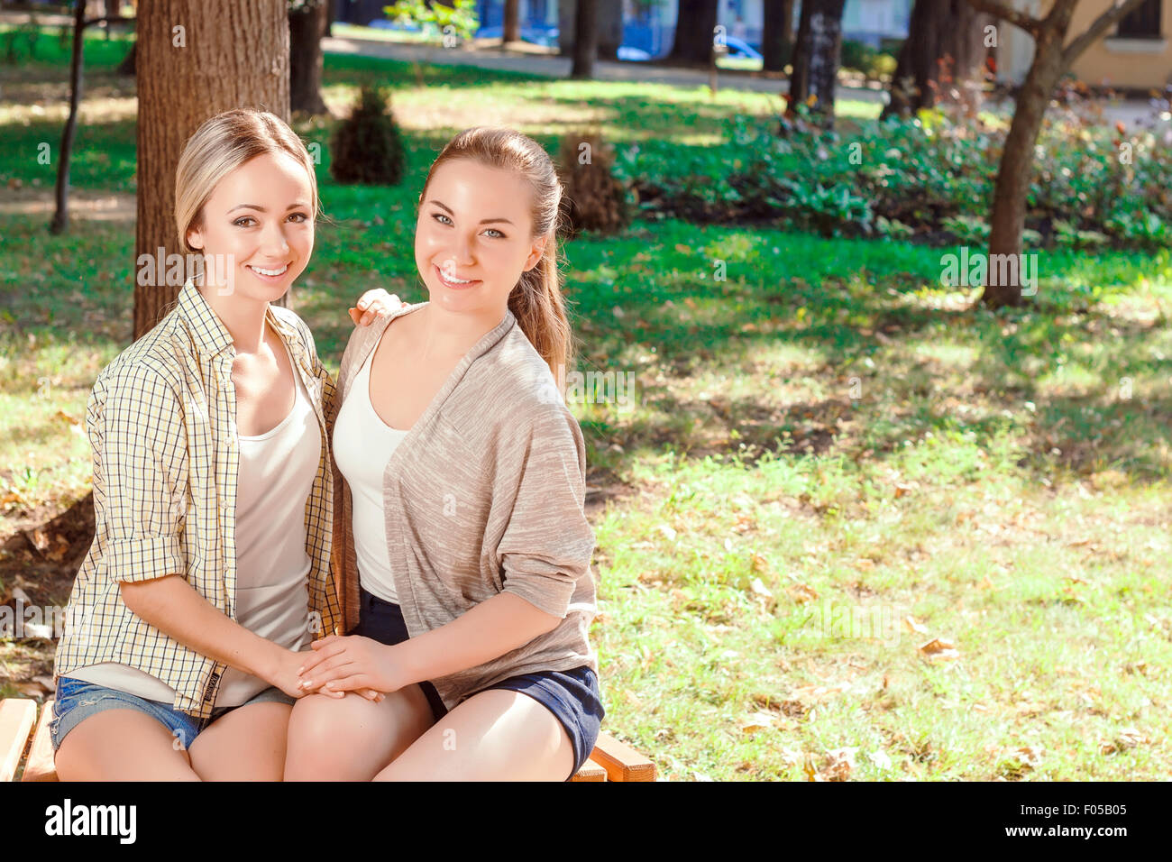 Two pretty girlfriends sitting in park Stock Photo - Alamy