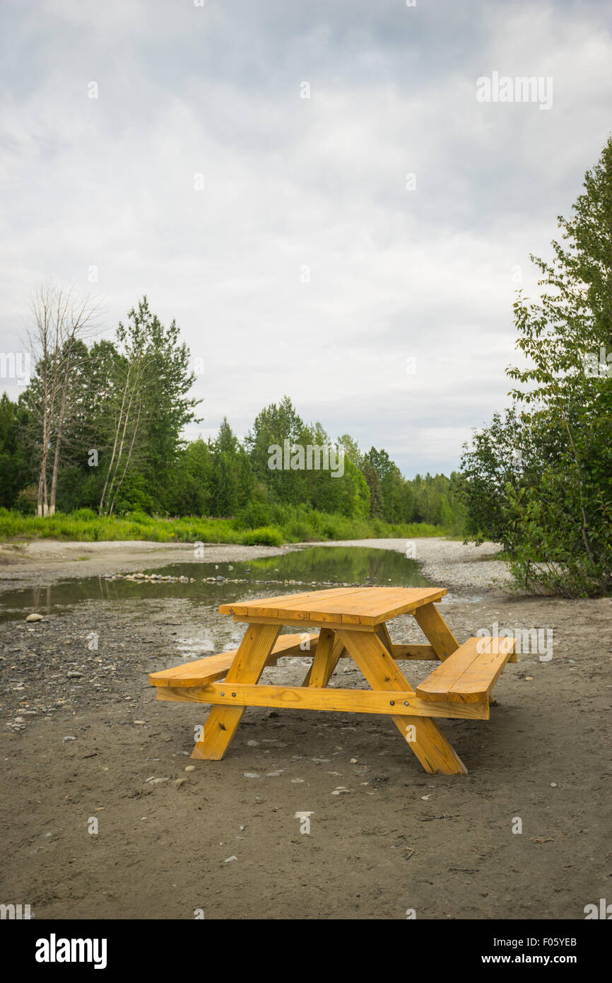 Wooden picnic table sits beside a stream in the Alaskan forest ...
