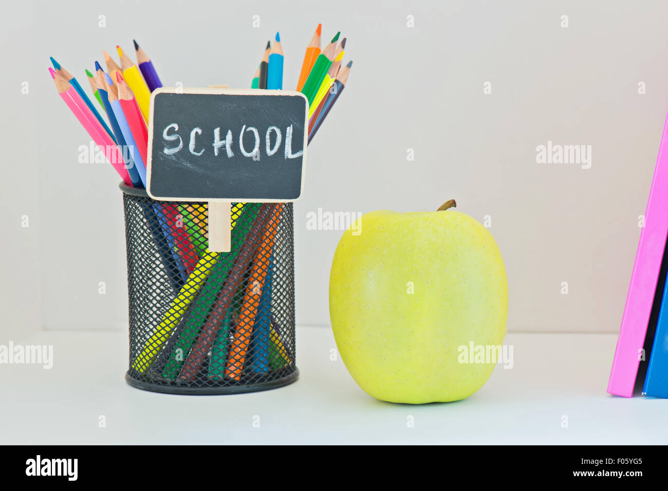 Concept of education. A yellow apple, pencils in case and multi colored books on the light ...