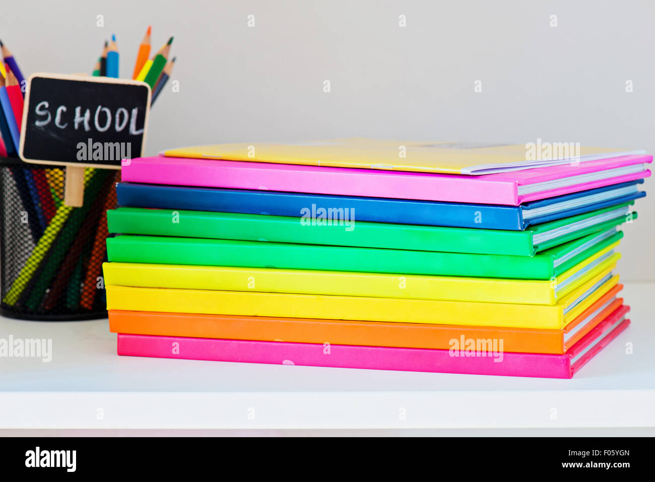 Multi colored books in stack on the light-coloured bookshelf and pencils in case on the ...