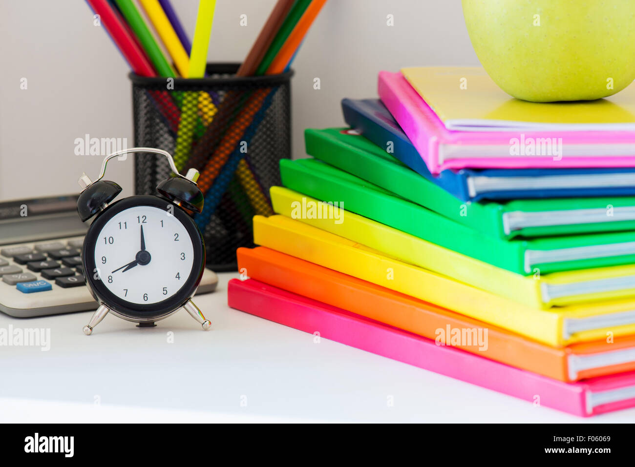 Concept of education. Black alarm clock. Multi colored books in stack on the light-coloured ...