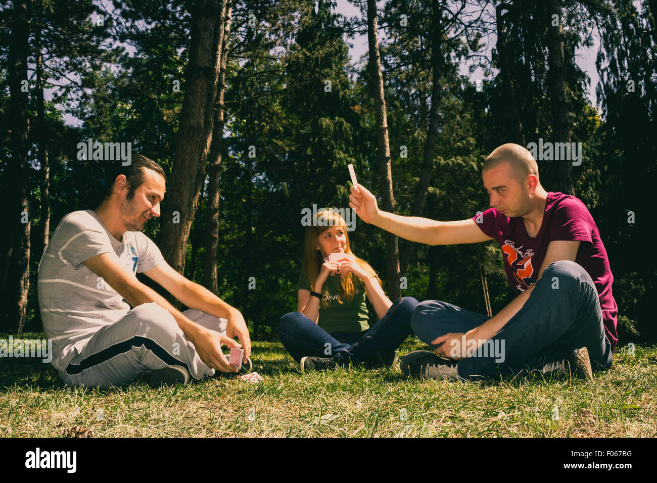 Three friends having fun by playing cards in the forest Stock Photo - Alamy