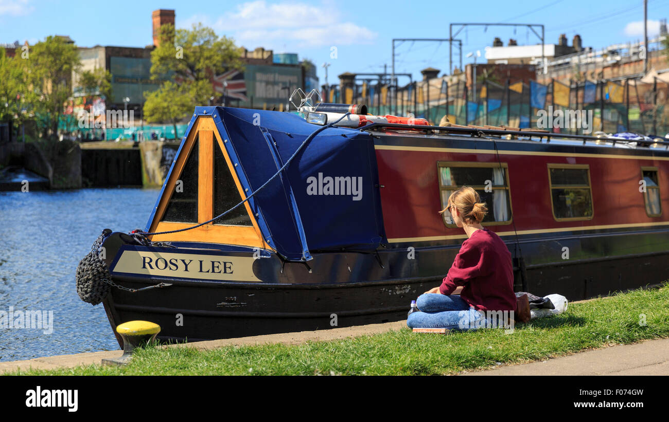 A young woman sits next to a narrow boat on the Regent's Canal between ...