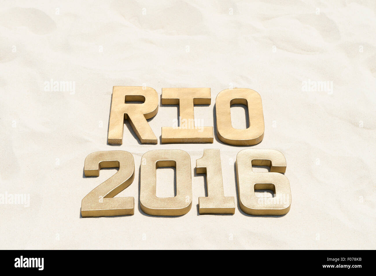 Golden Rio 2016 sign sitting on smooth sand beach background in Rio de ...