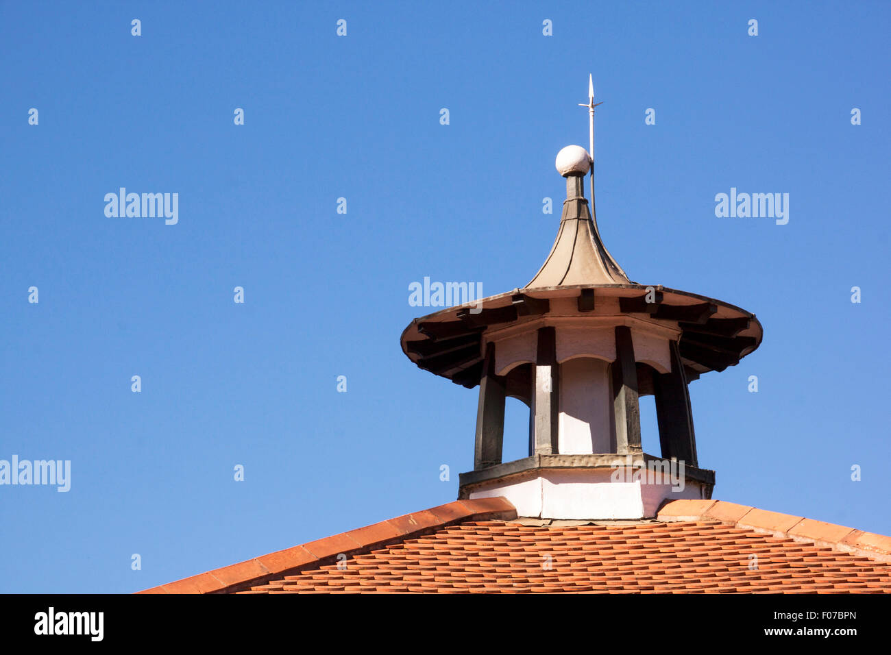 Close up turret extending from red tiled roof against clear blue sky ...