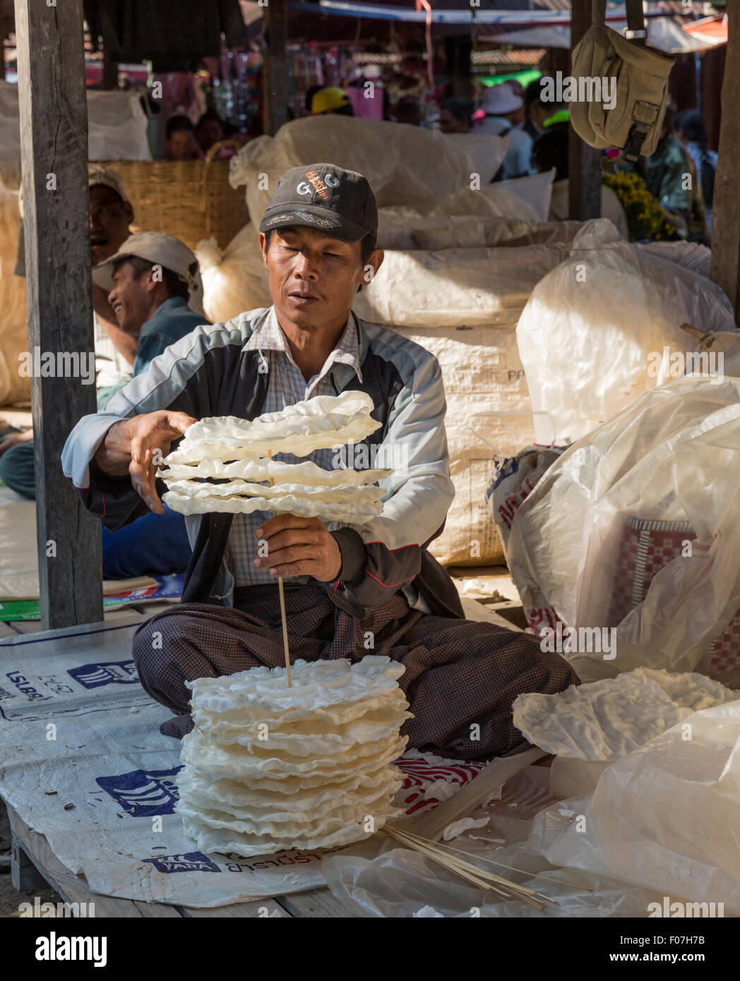 Vendor at Nam Pan five day market stacking papadams on a spike before ...