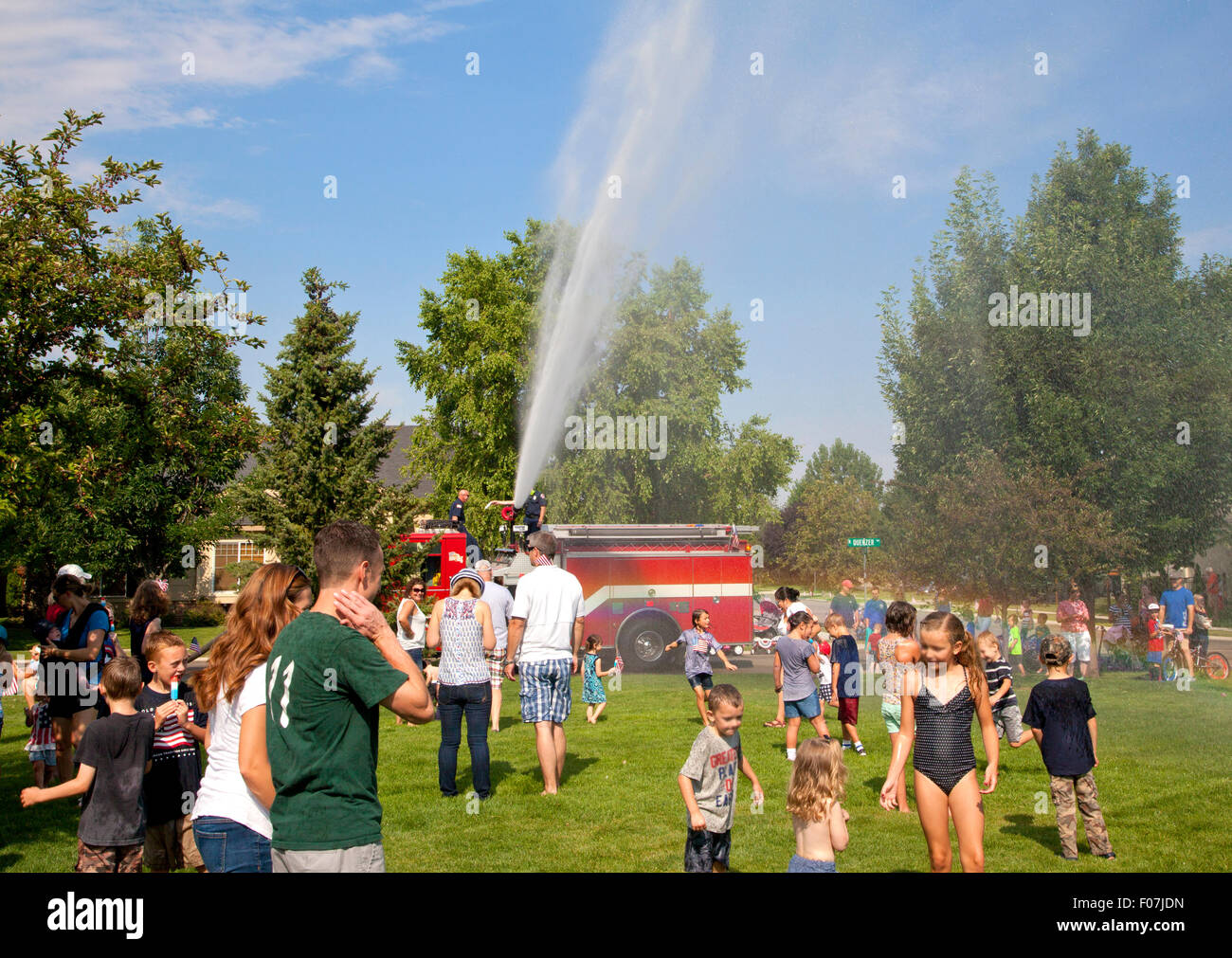 Crowd enjoys water spray from a firetruck, July Fourth celebration, USA ...