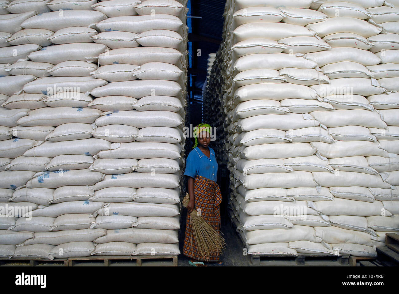 A woman stands amid large sacks of basic foodstuffs at a storage ...
