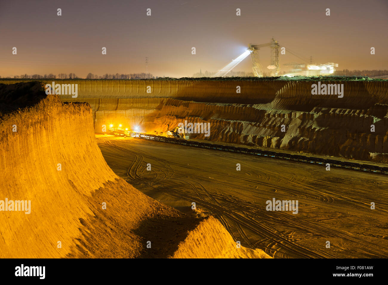 A steep lignite pit mine wall illuminated at night with an excavator in ...
