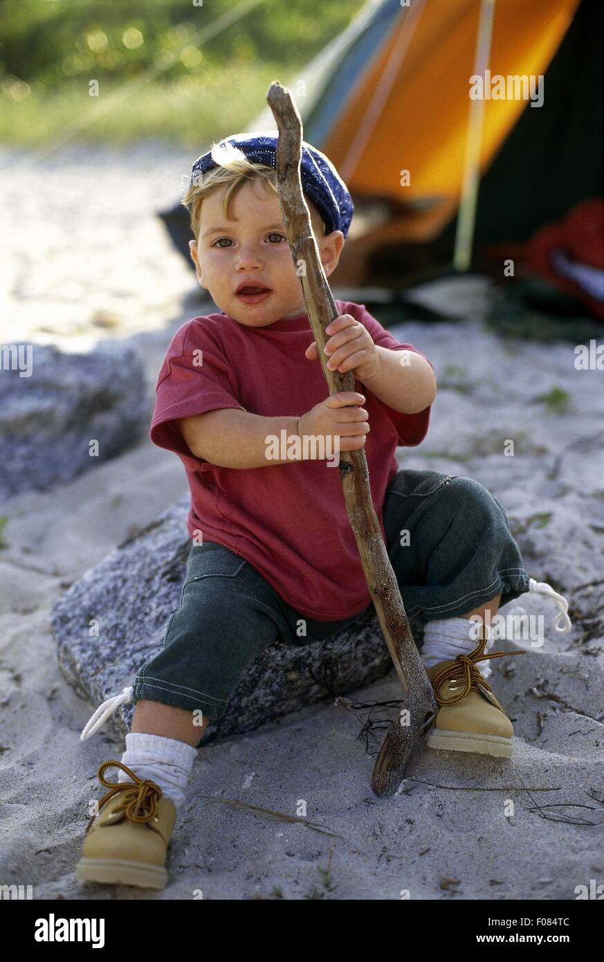 Child sitting on stone and holding stick Stock Photo - Alamy